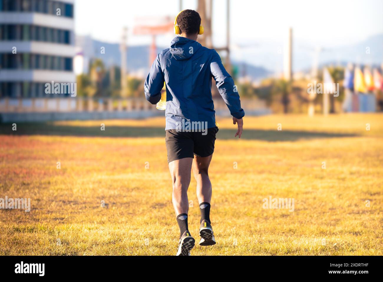 Rear view jockster running through city streets, with a bottle of water ...