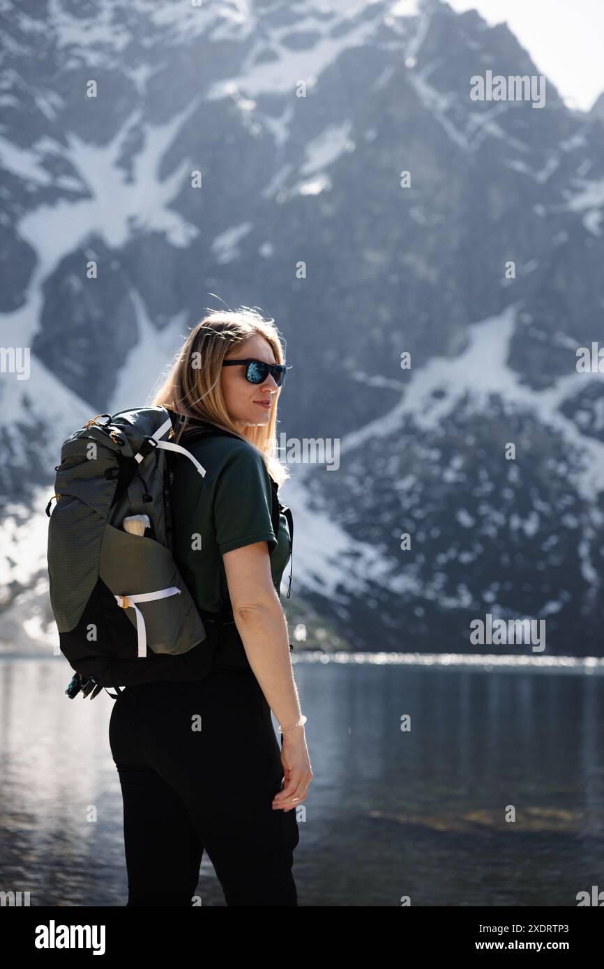 A traveler girl with a backpack enjoys the stunning view of a mountain ...
