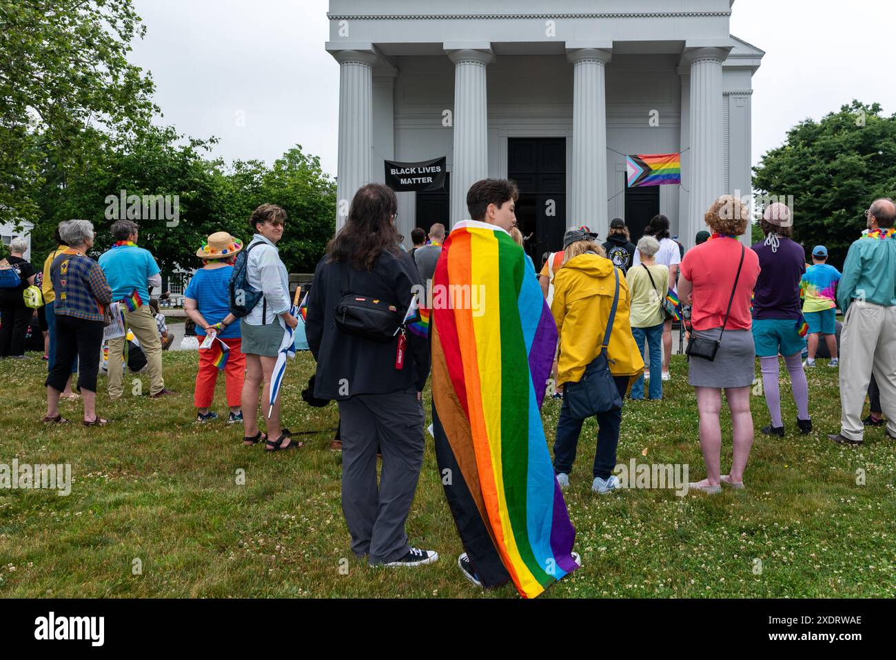 Young man wearing a Pride flag, standing with a crowd at the First ...