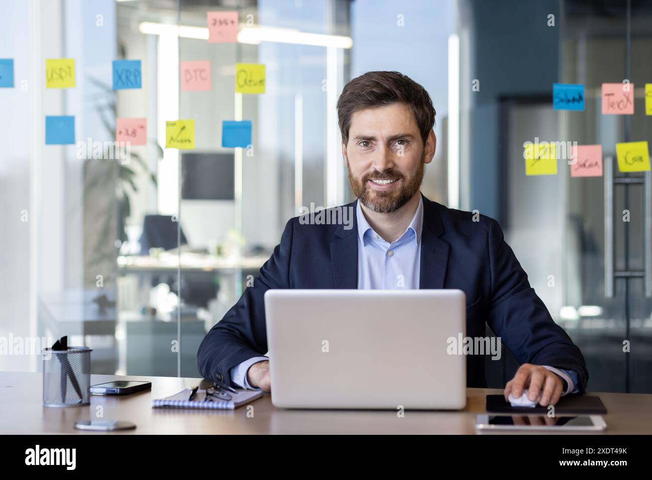 Confident businessman in suit smiling while working on laptop in modern ...