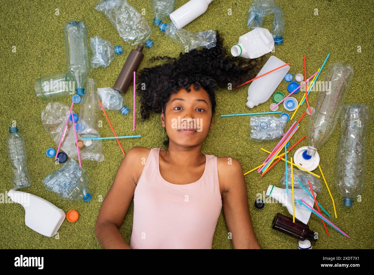 Woman lies on green carpet surrounded by various plastic waste items ...