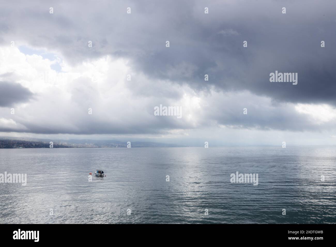 A small boat floating on a calm sea under a dramatic cloudy sky with a ...