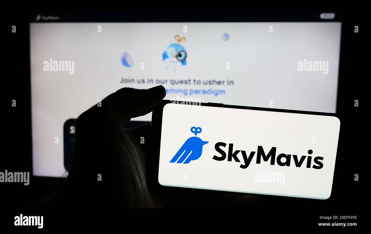 Person holding mobile phone with logo of video games company Sky Mavis Pte. Ltd. in front of ...