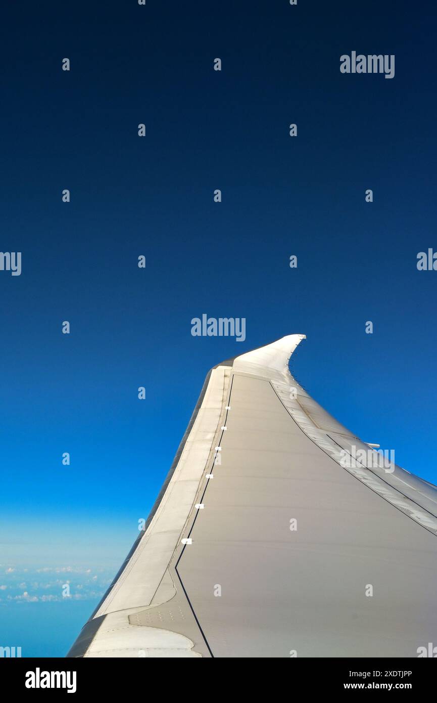 Wing of a modern passenger jet in flight isolated against a deep blue ...