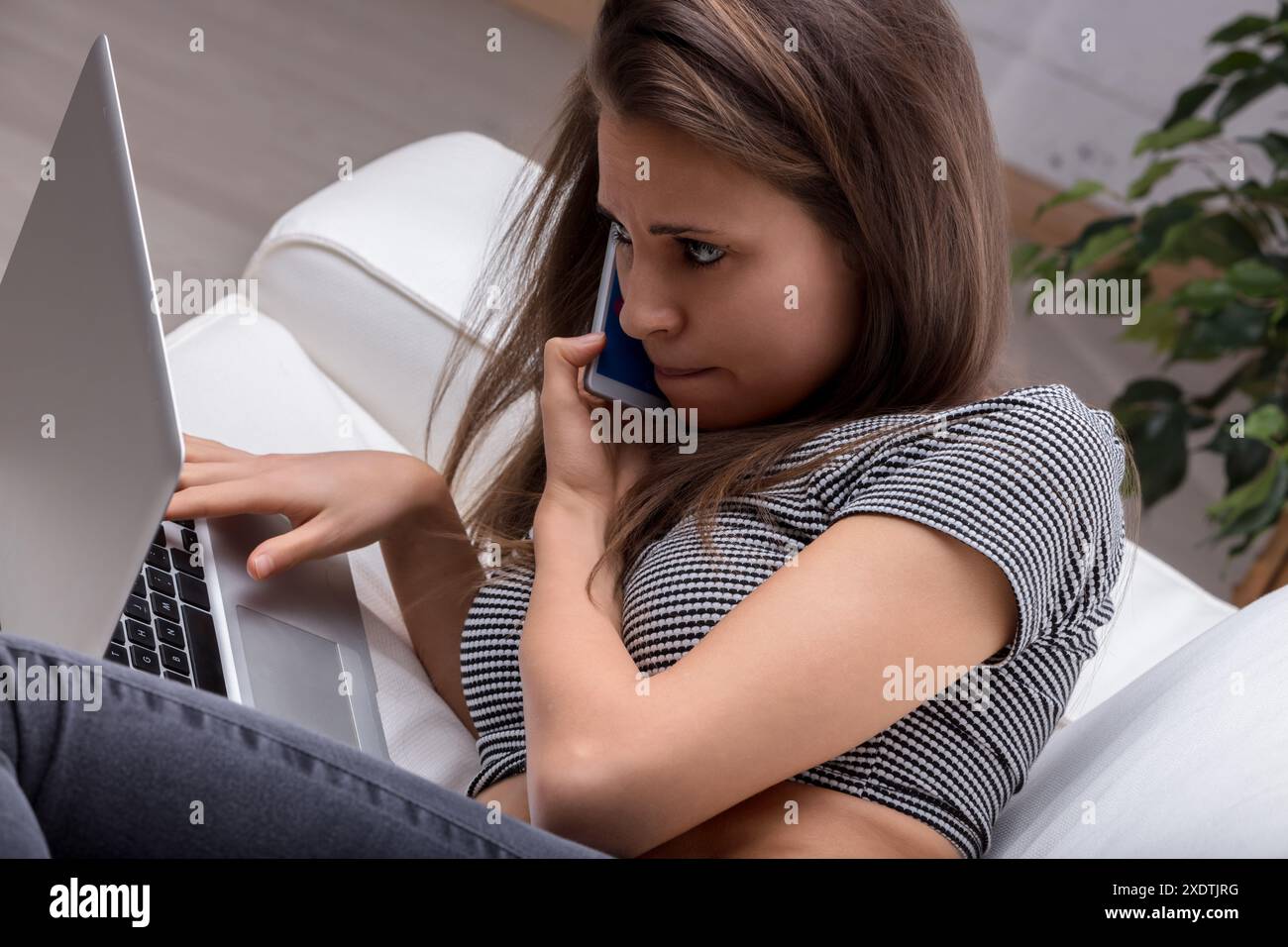 Stressed young woman multitasking on a sofa with laptop and phone ...