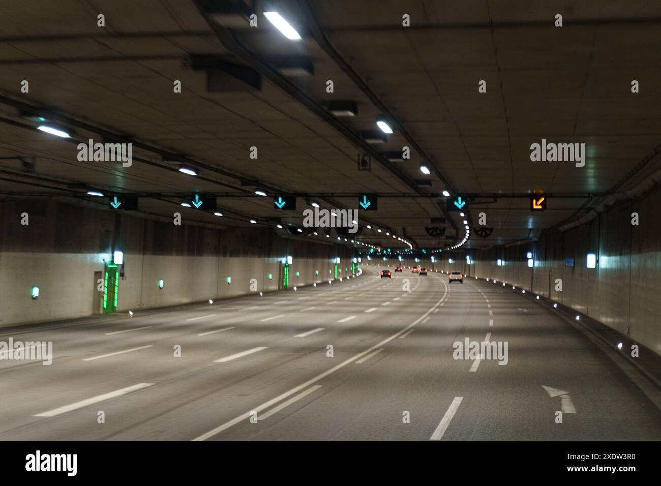 A long, empty highway tunnel with fluorescent lights and downward arrow ...