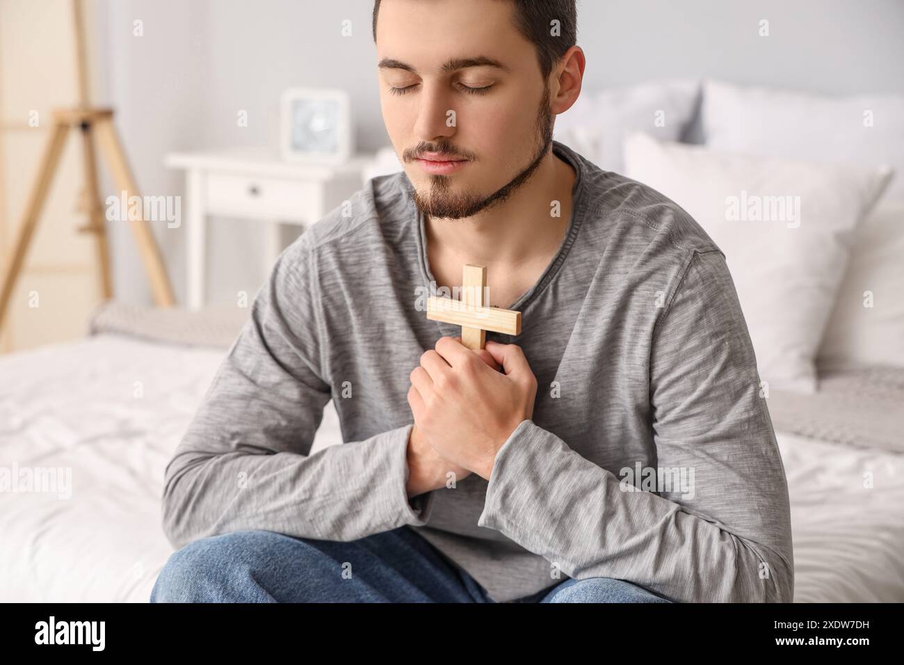 Young man with wooden cross praying in bedroom Stock Photo - Alamy