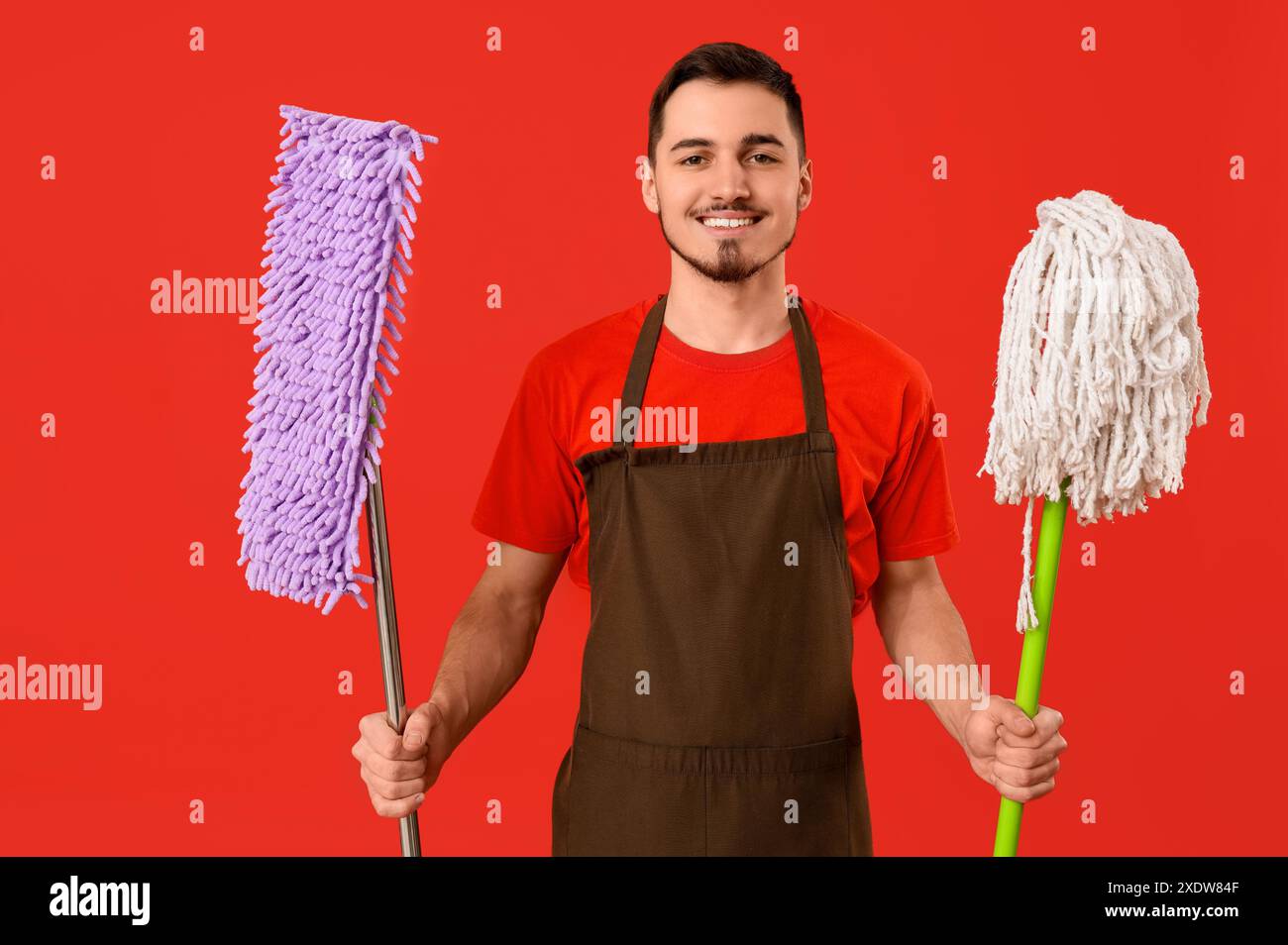 Male janitor with floor mops on red background Stock Photo - Alamy