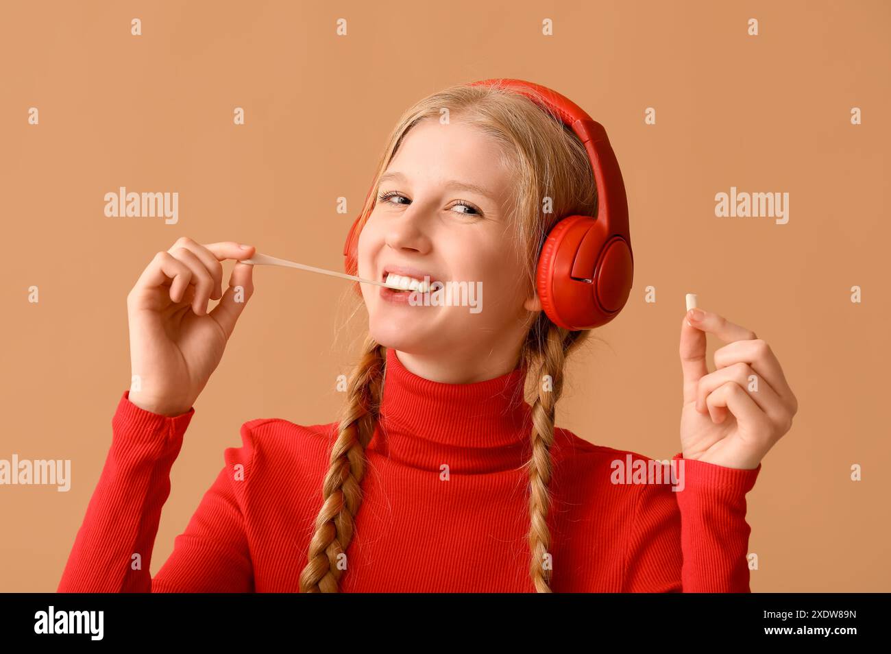 Teenage girl in headphones chewing gum on beige background, closeup ...