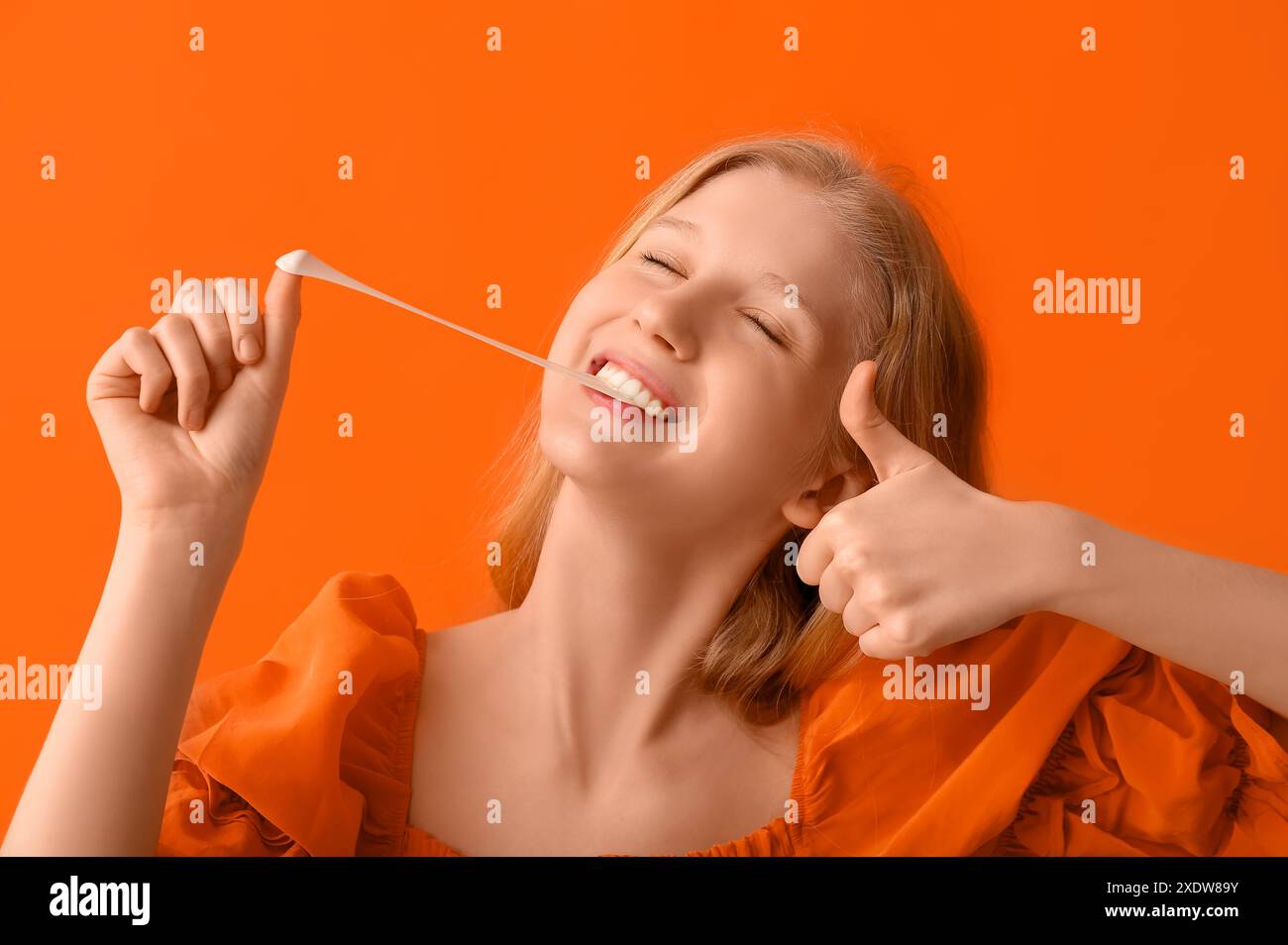 Teenage girl with chewing gum showing thumb-up on orange background ...