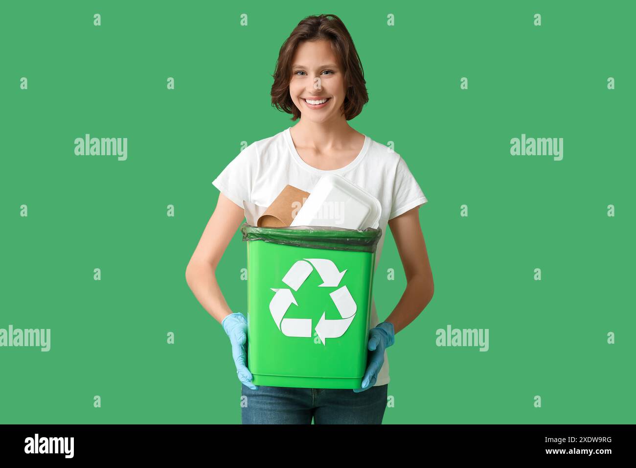 Female volunteer holding recycle bin with garbage on green background ...