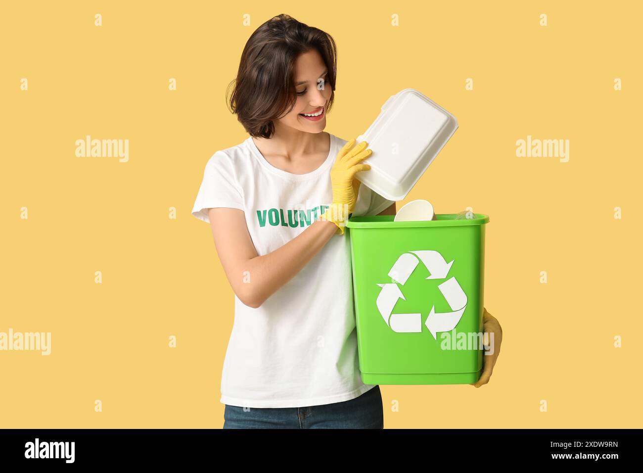 Female volunteer holding recycle bin with garbage and plastic container ...