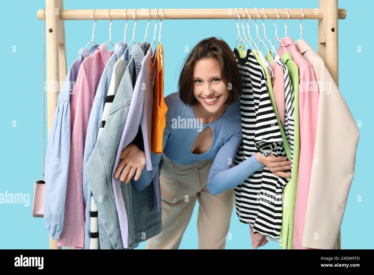Beautiful young woman near rack with different clothes on blue ...