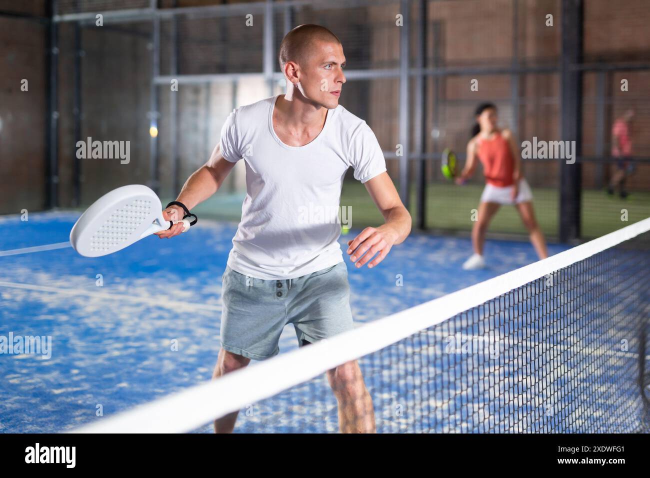 Padel player playing padel in a padel court indoor behind net Stock ...