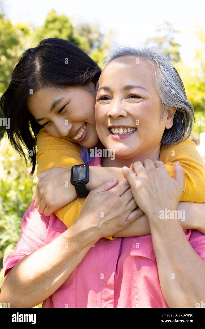 Asian woman hugging senior mother from behind, both smiling in outdoor ...