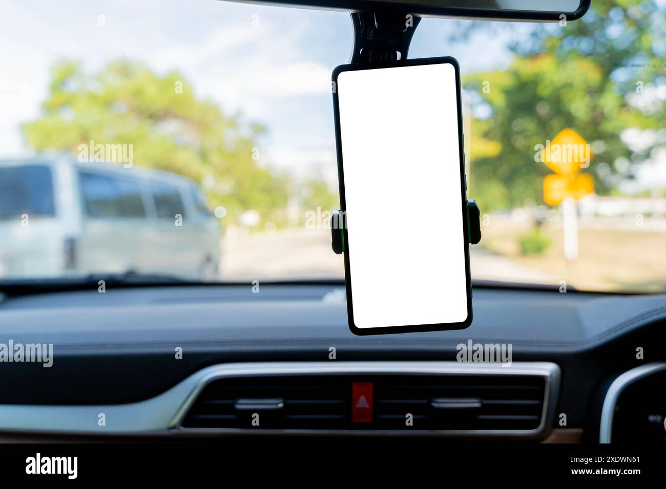 A blank white screen smartphone on a car dashboard with a scenic road ...