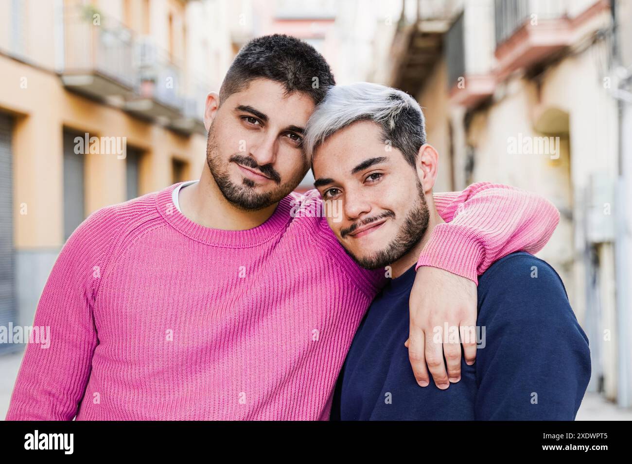 Gay couple smiling on camera on city street. Male lovers hug each other. LGBT life style concept ...