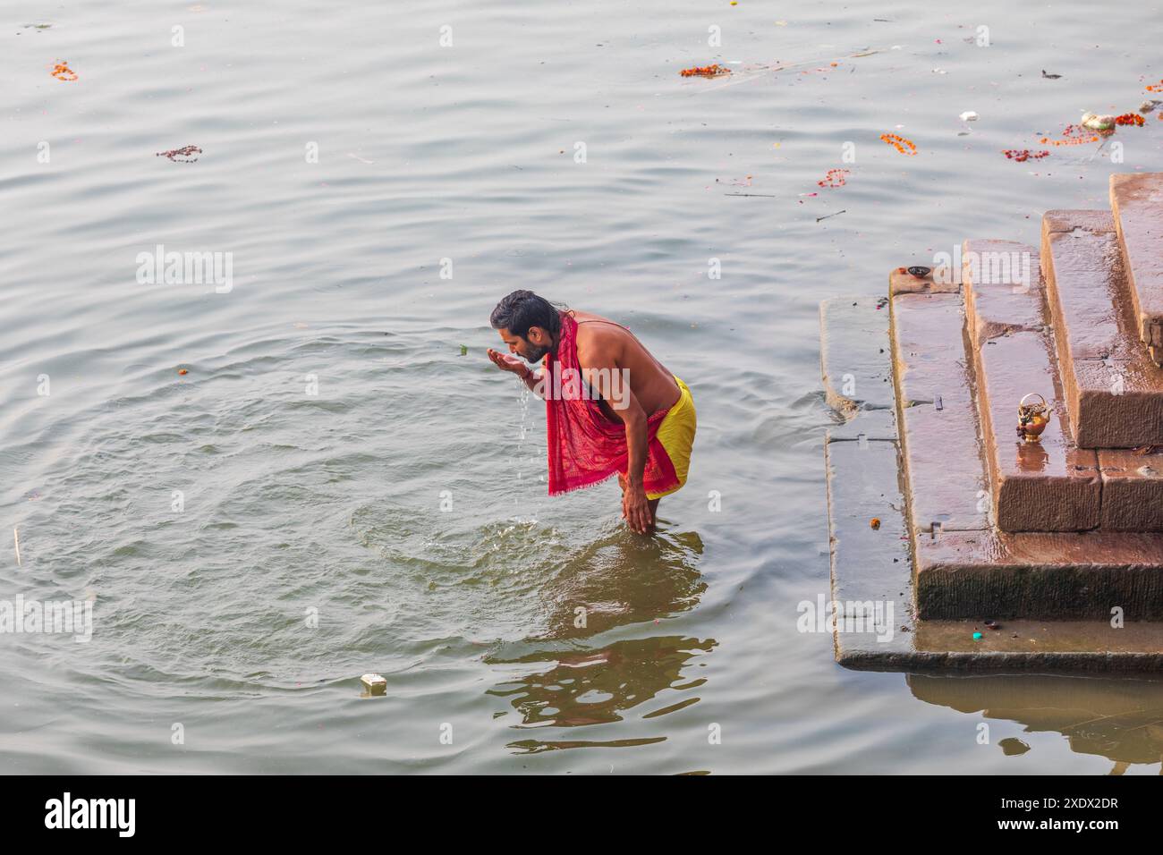 India, Uttar Pradesh, Varanasi. A man on the steps of a ghat washes in ...