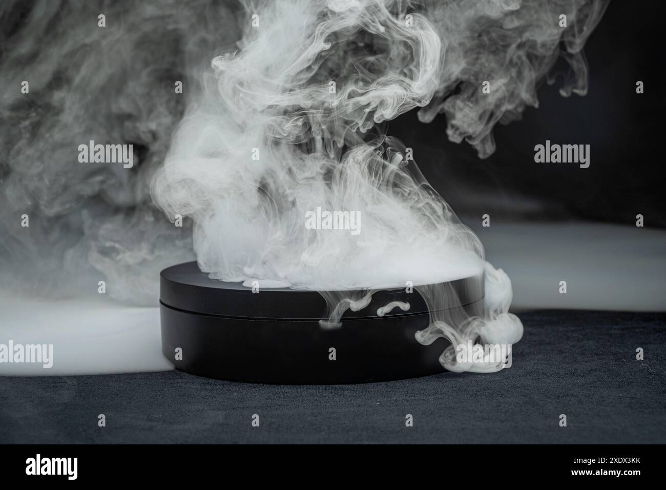 White smoke is emanating from a round black box on a dark background ...
