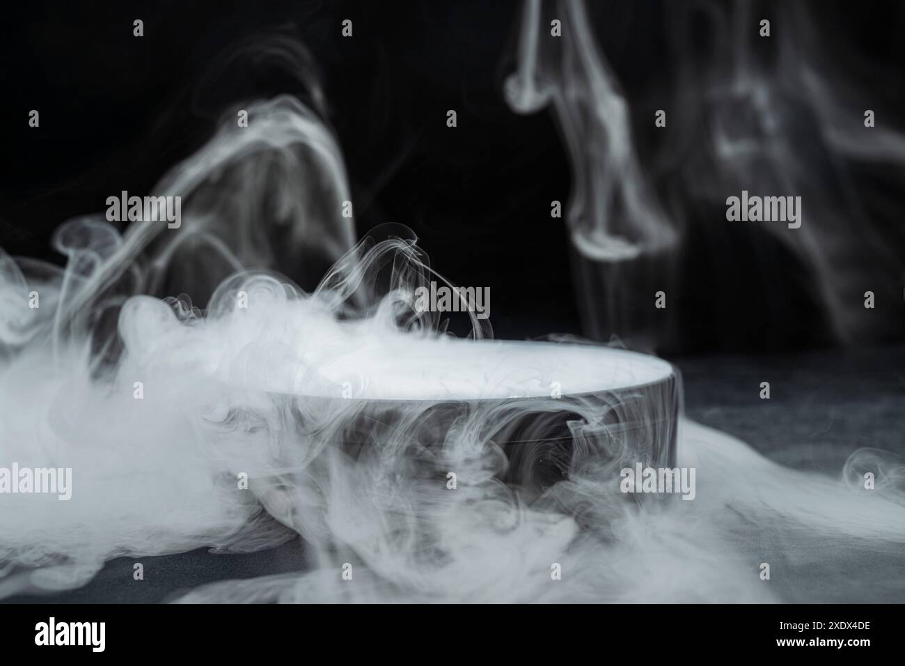 White smoke flows from a circular container against a black backdrop ...