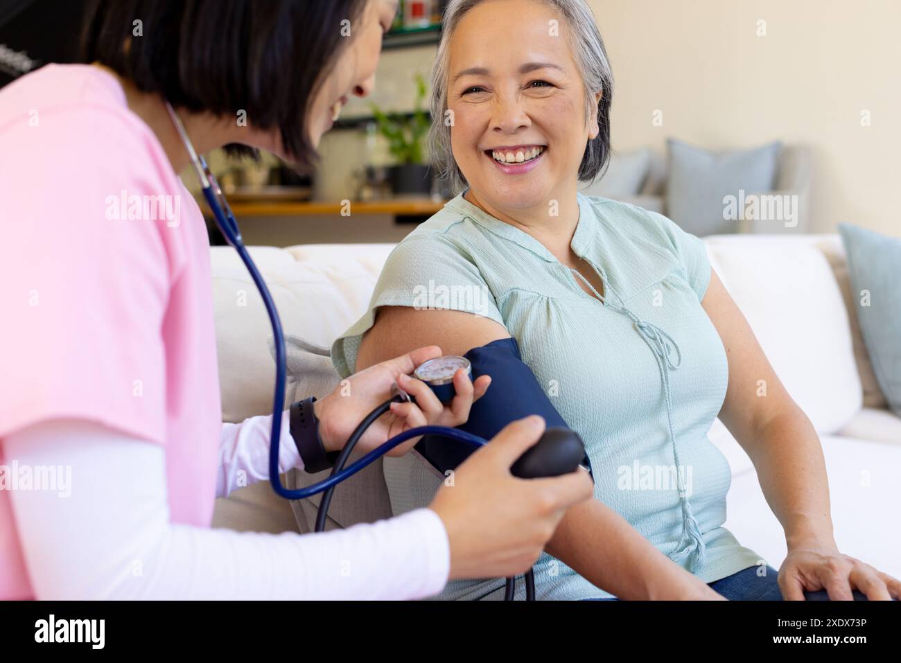 Female nurse checking blood pressure of senior Asian woman, smiling on ...