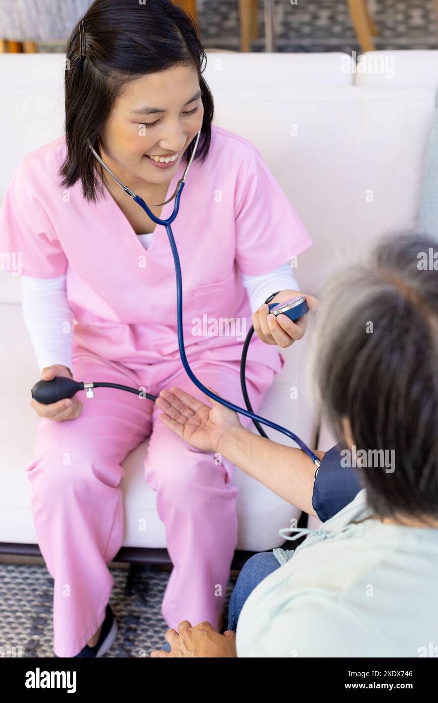 Female nurse in pink scrubs checking blood pressure of senior patient ...