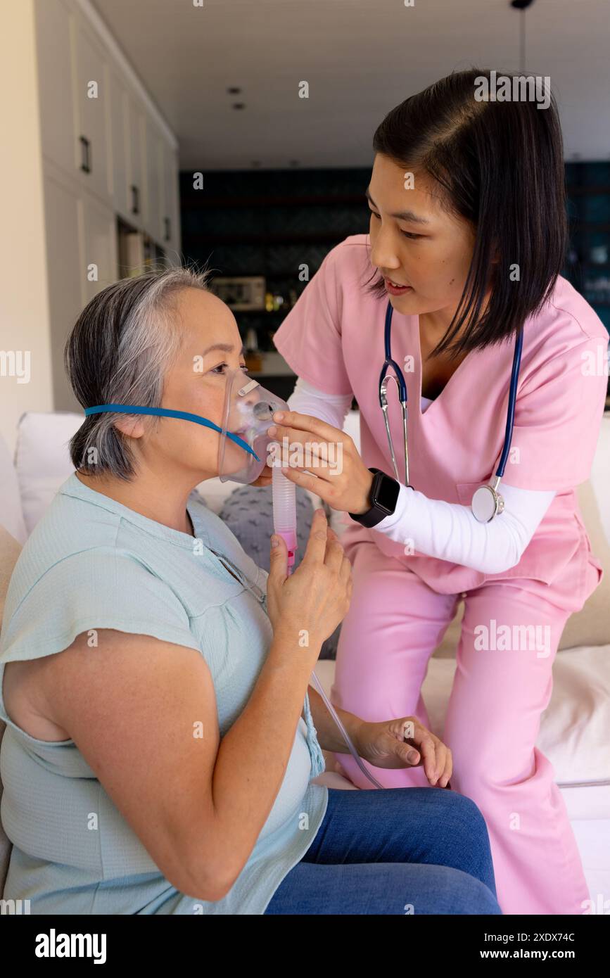 Female nurse in pink scrubs assisting senior woman with oxygen mask at ...