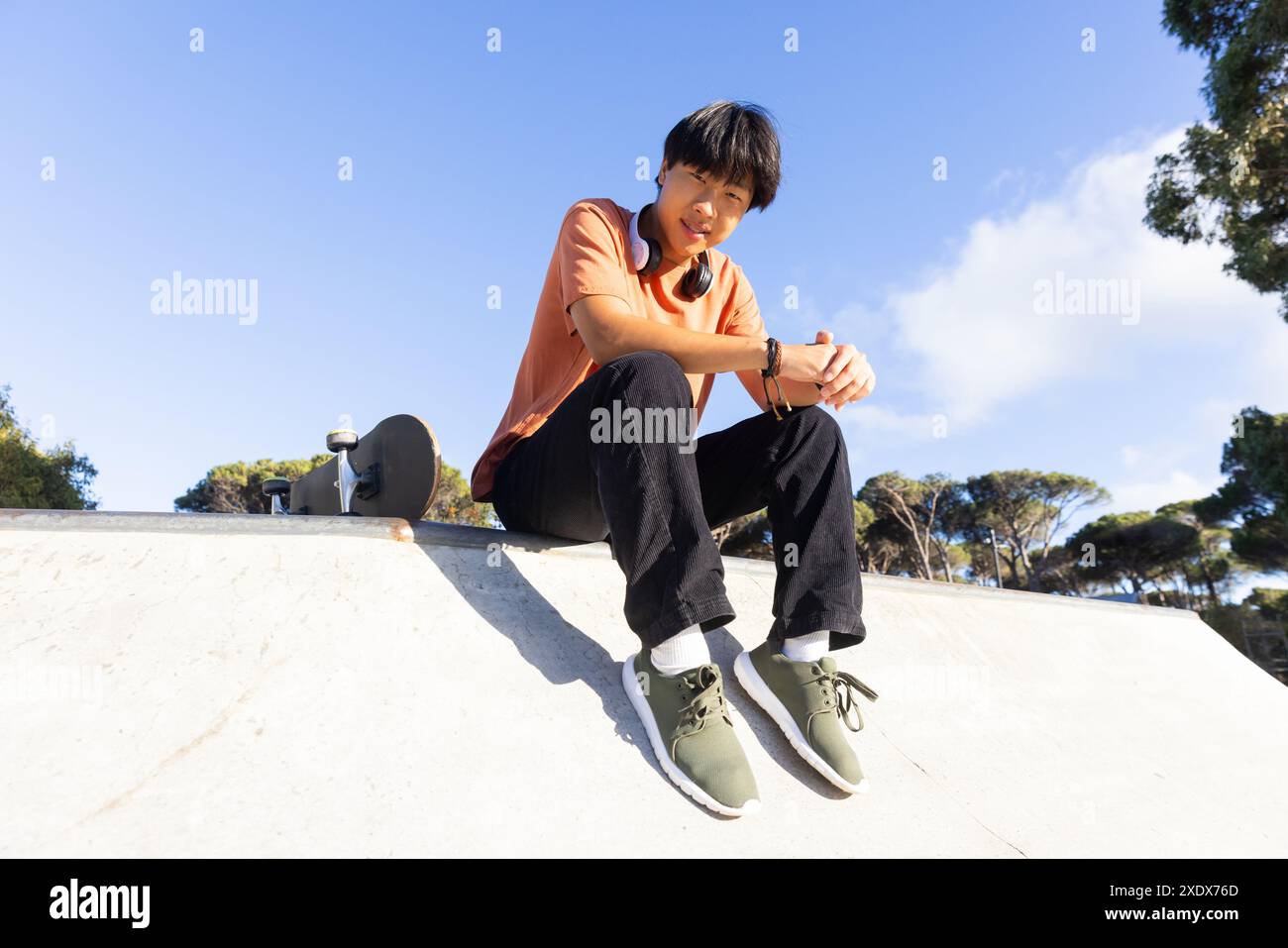 Teenage boy sitting on skateboard ramp with headphones, enjoying ...