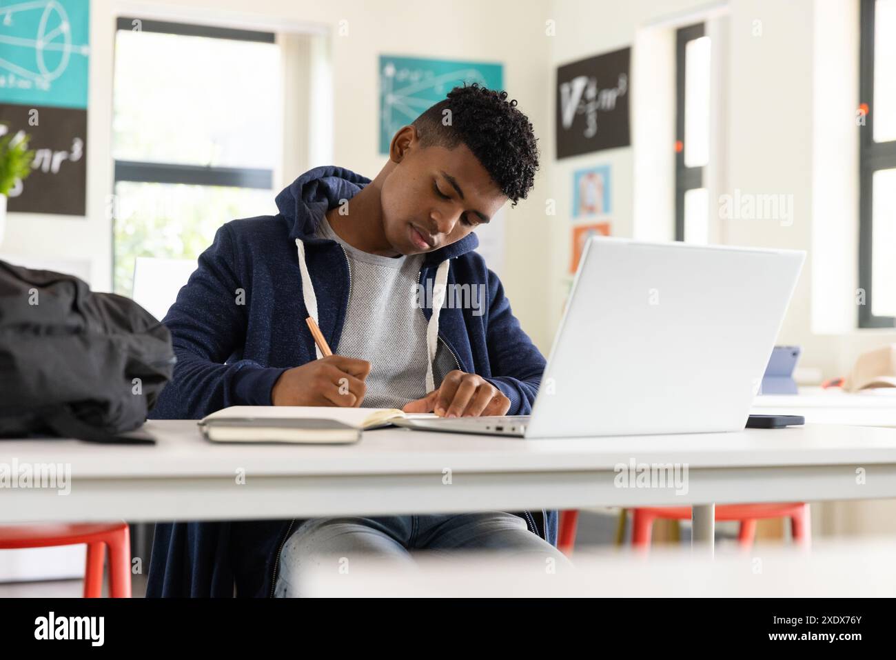 In school, African American male student writing in notepad and using ...
