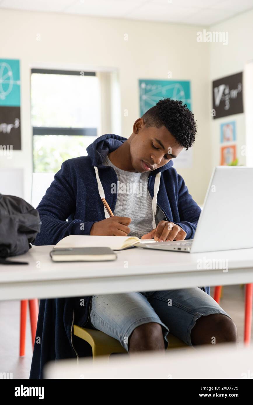 Writing in notebook and using laptop, African American male student in ...