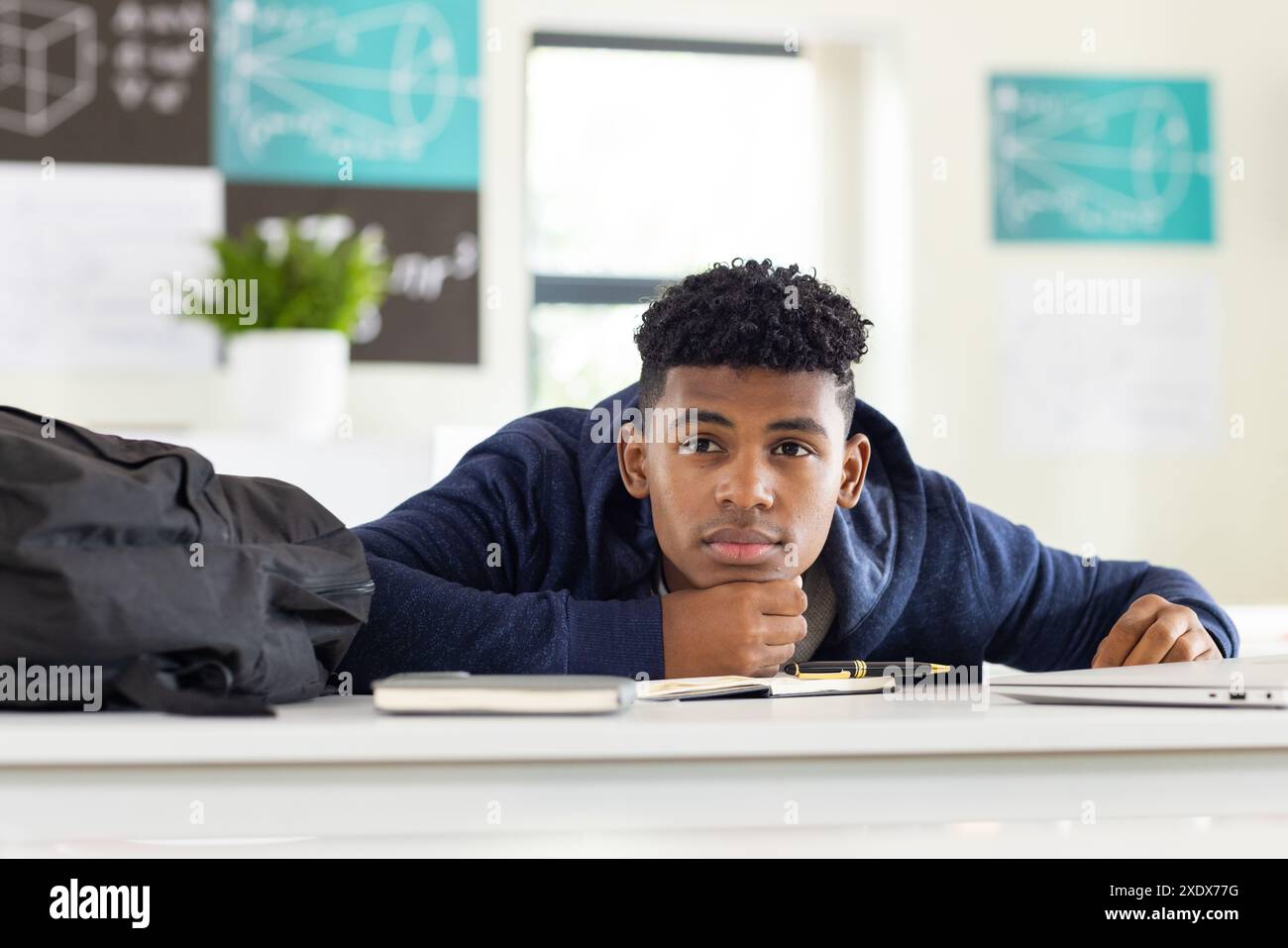 In school, African American teenage boy resting head on desk, looking ...