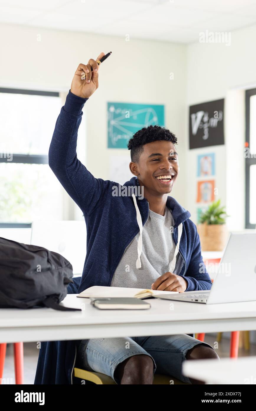 In school, male student raising hand while using laptop in classroom ...