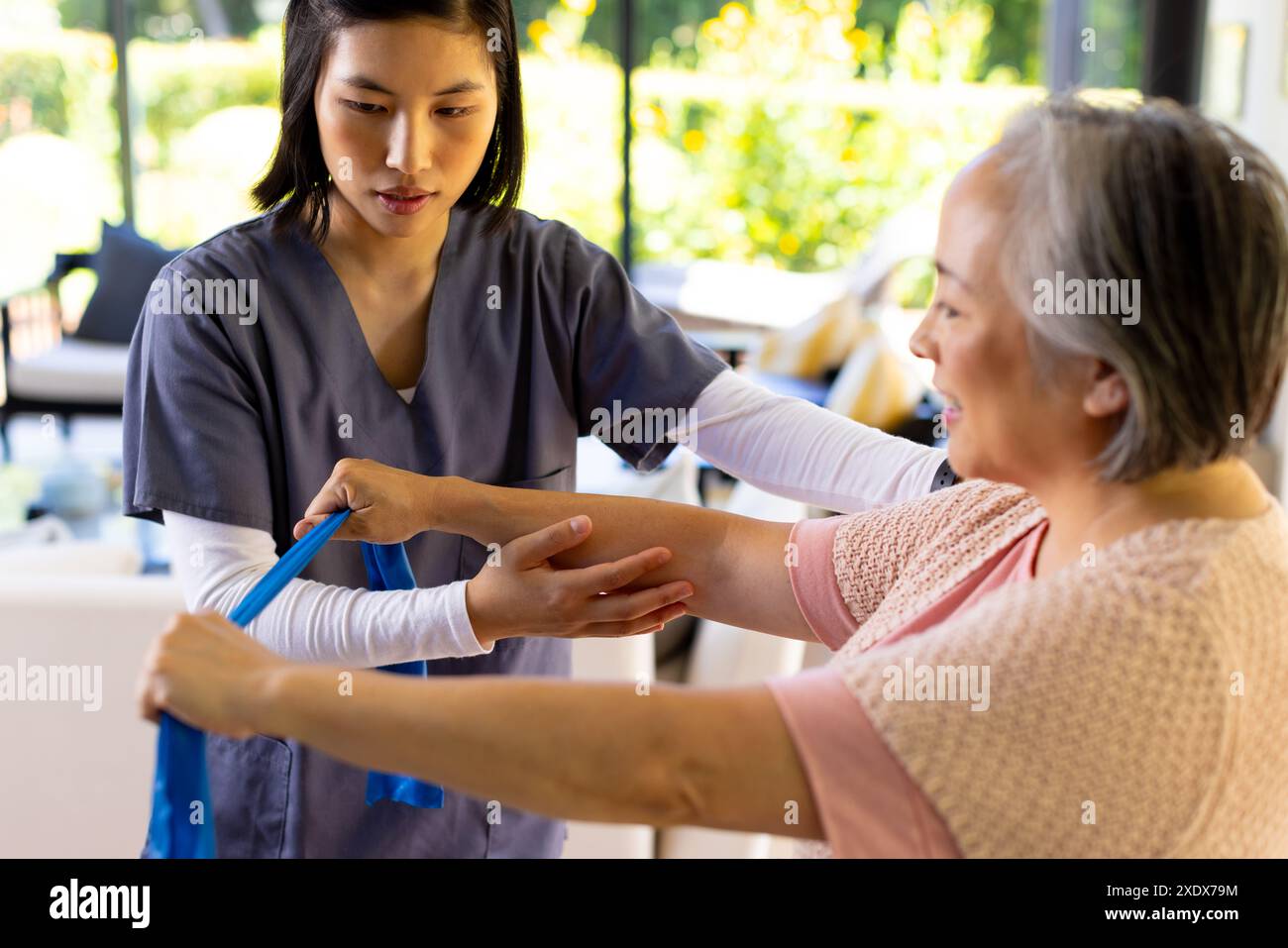 Asian female nurse assisting senior woman with resistance band exercise ...