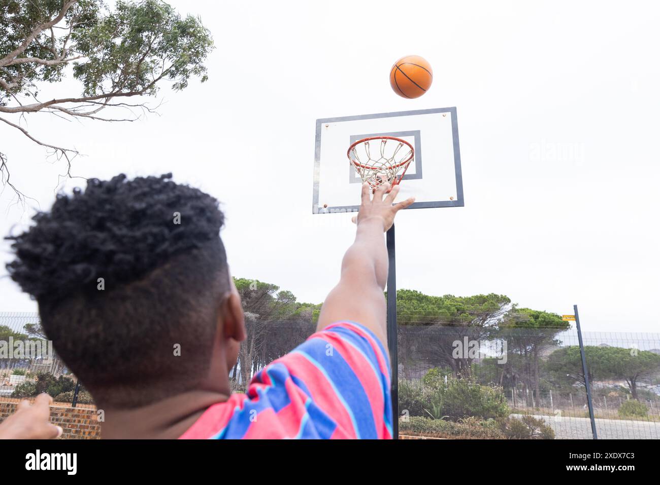 Playing basketball, male student shooting ball towards hoop in outdoor ...