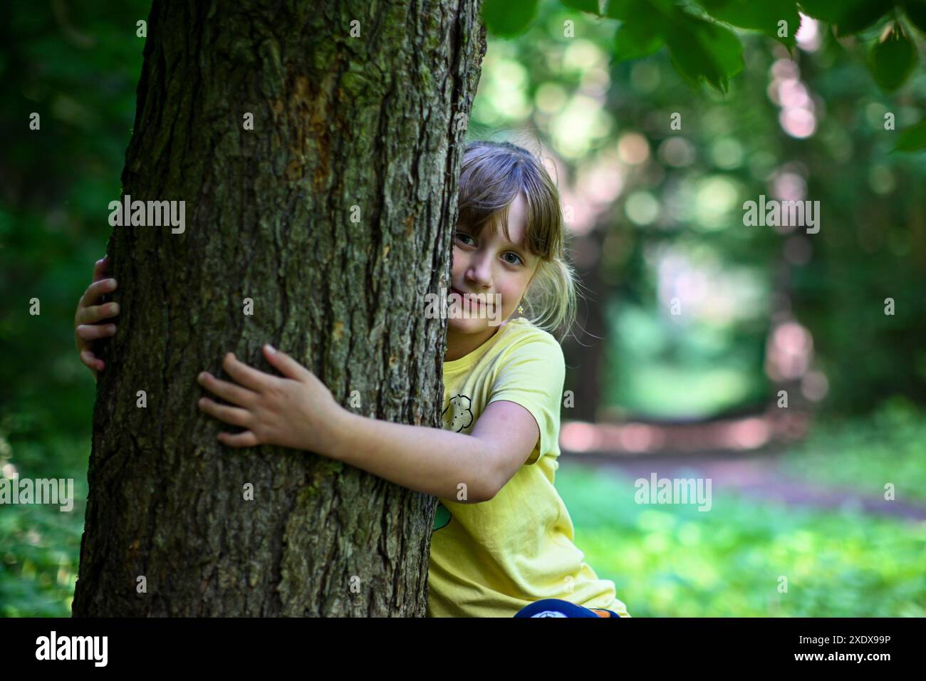 Young girl is embracing a large tree in a forest showing her love and ...