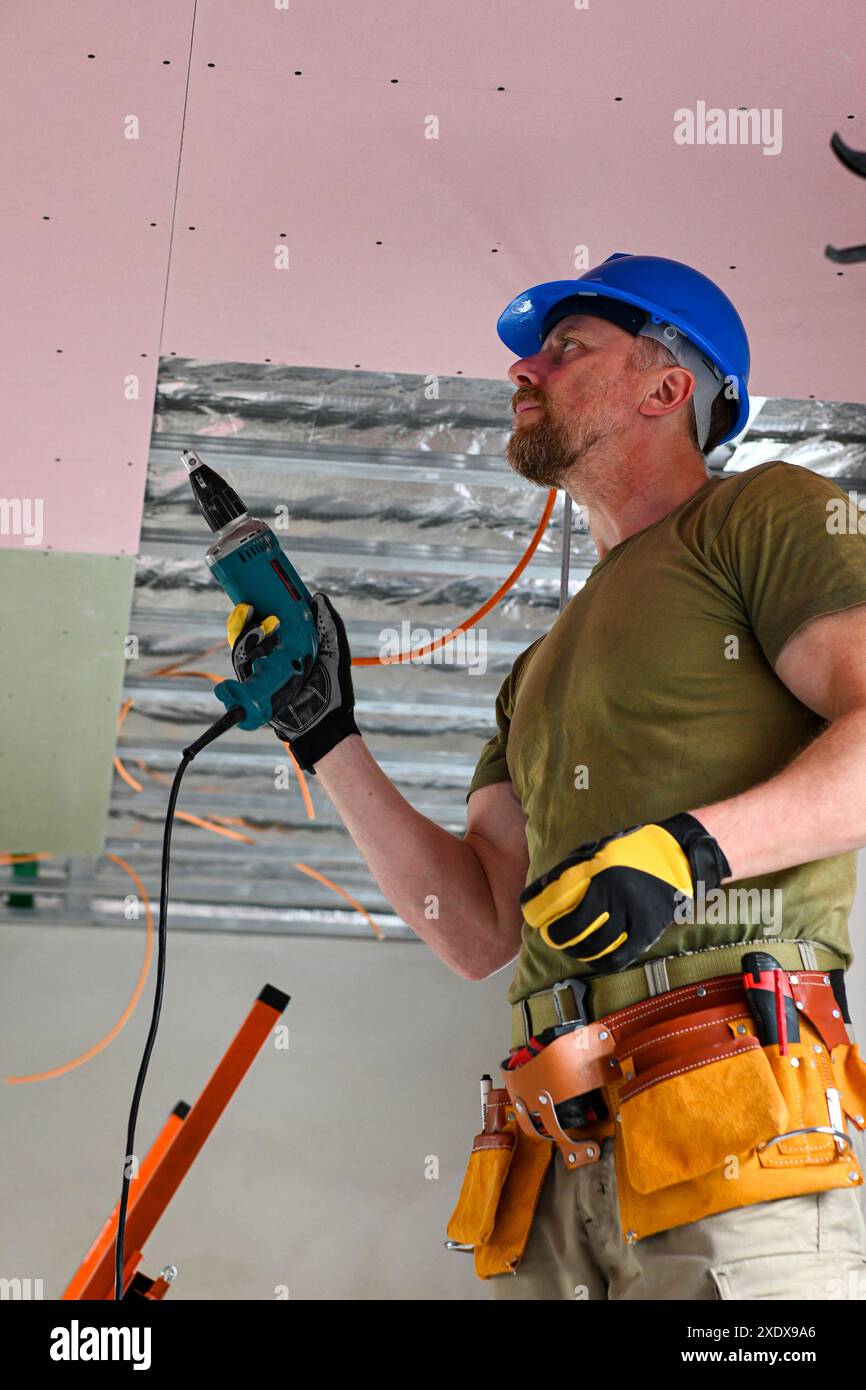 Construction worker wearing tool belt and safety equipment using power ...