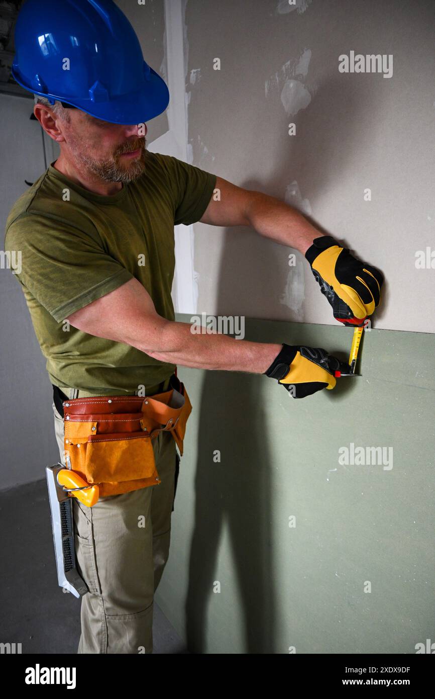 Construction worker wearing tool belt and hard hat measuring ...