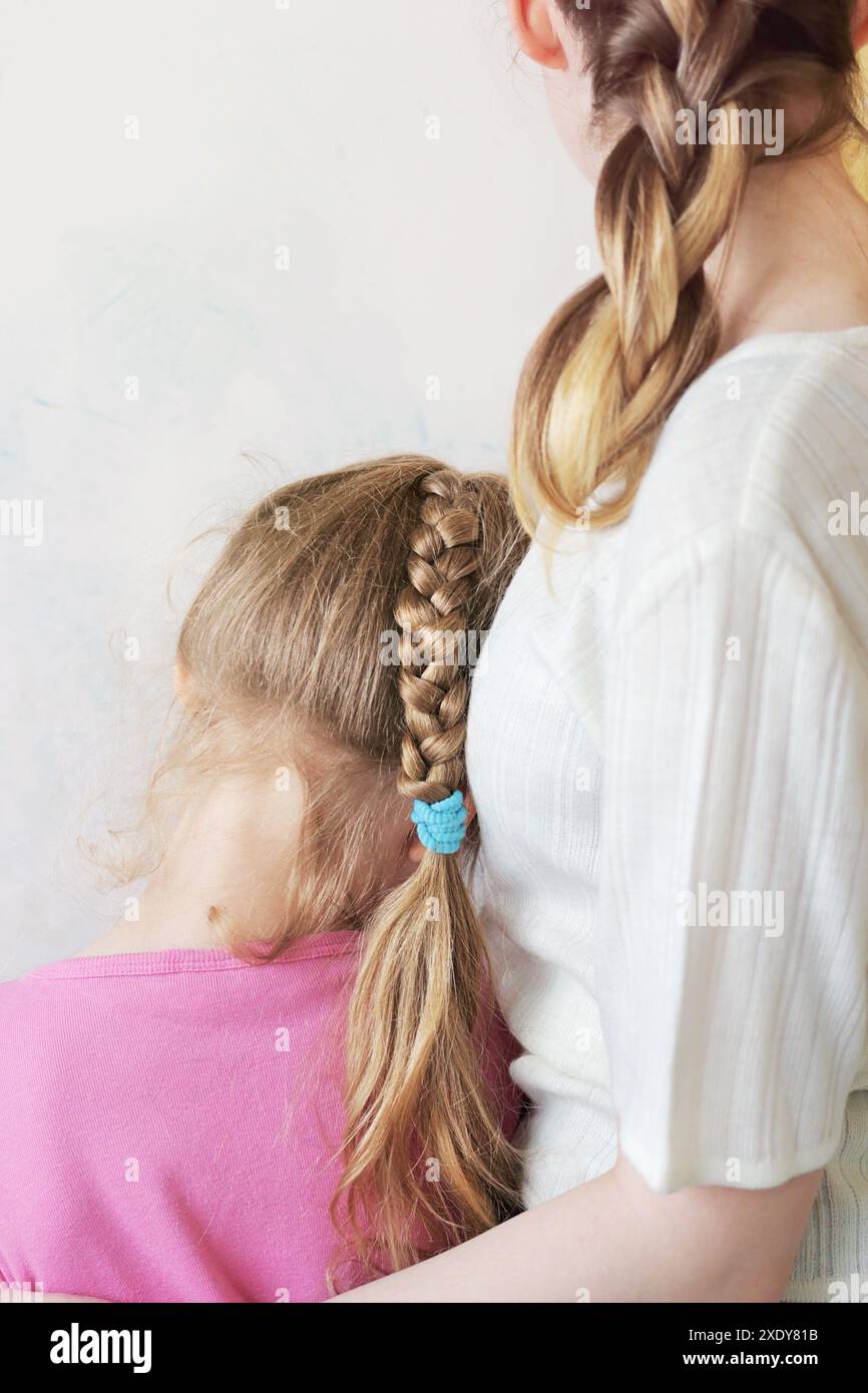 A young girl with a plait hugs a little girl with a long light braid ...