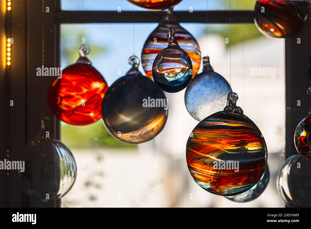 Colorful transparent glass balls hang in front of bright window ...