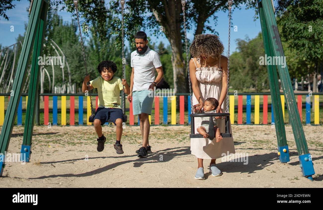 Family with two children, a boy and a baby swinging on some swings in a children's park Stock ...