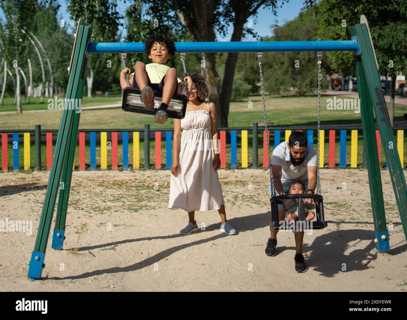 Latin family swinging their two children on swings in a park. Mother ...