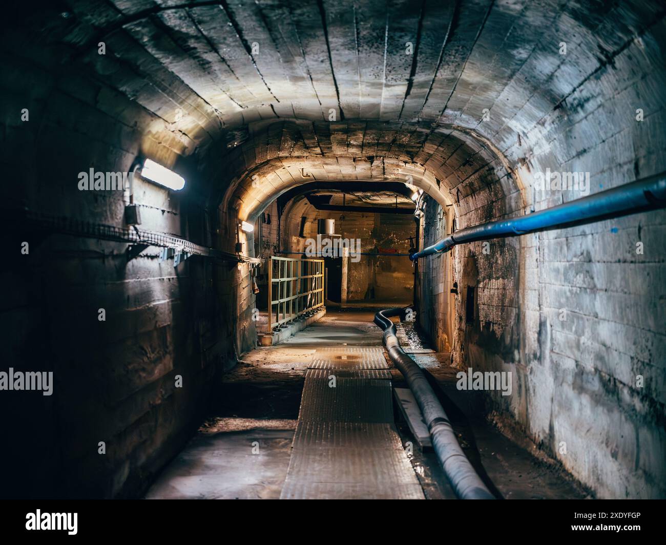 Industrial underground tunnel with metal walkway and pipes, illuminated ...