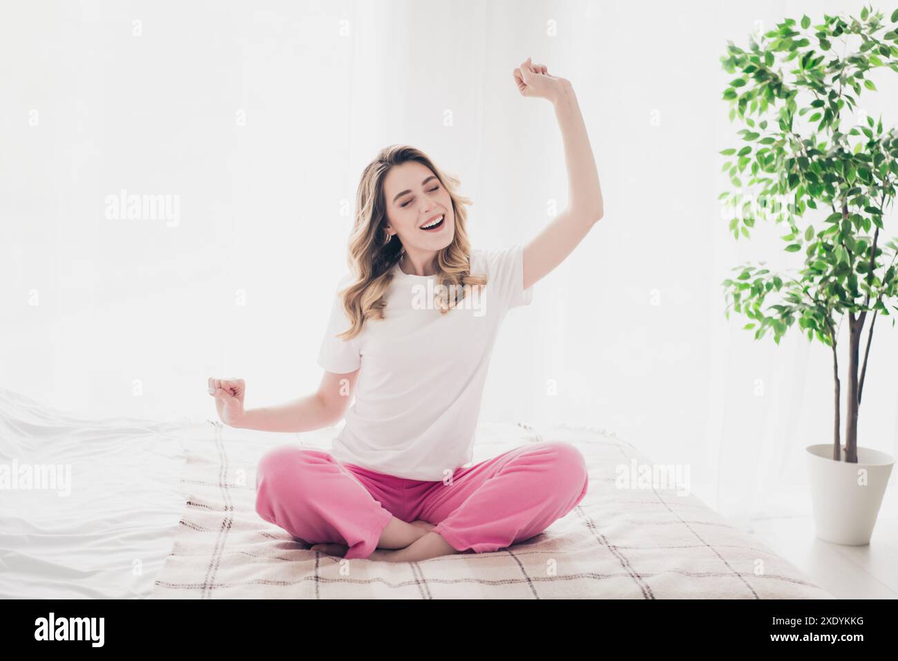 Photo of positive girl sit bed yawn stretching hands up in white room ...