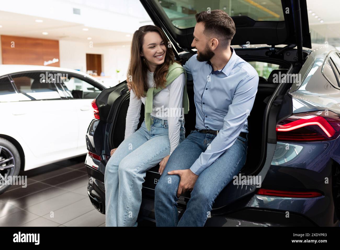 Happily young couple sitting in car trunk dangling legs in car ...