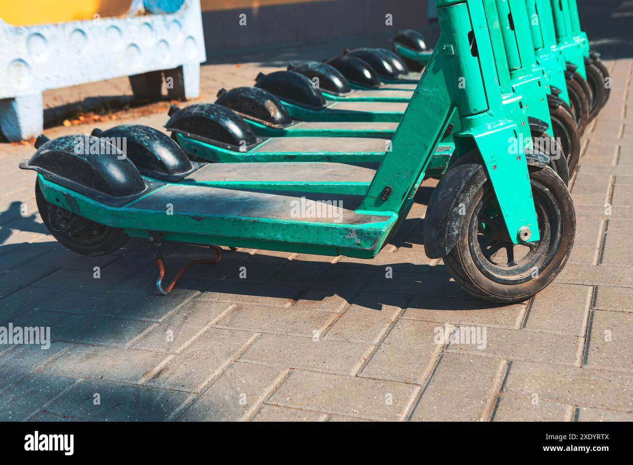 Row of green scooters are parked on a brick sidewalk. The scooters are ...