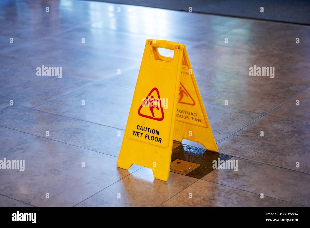There is a yellow caution wet floor sign placed on a tiled floor ...