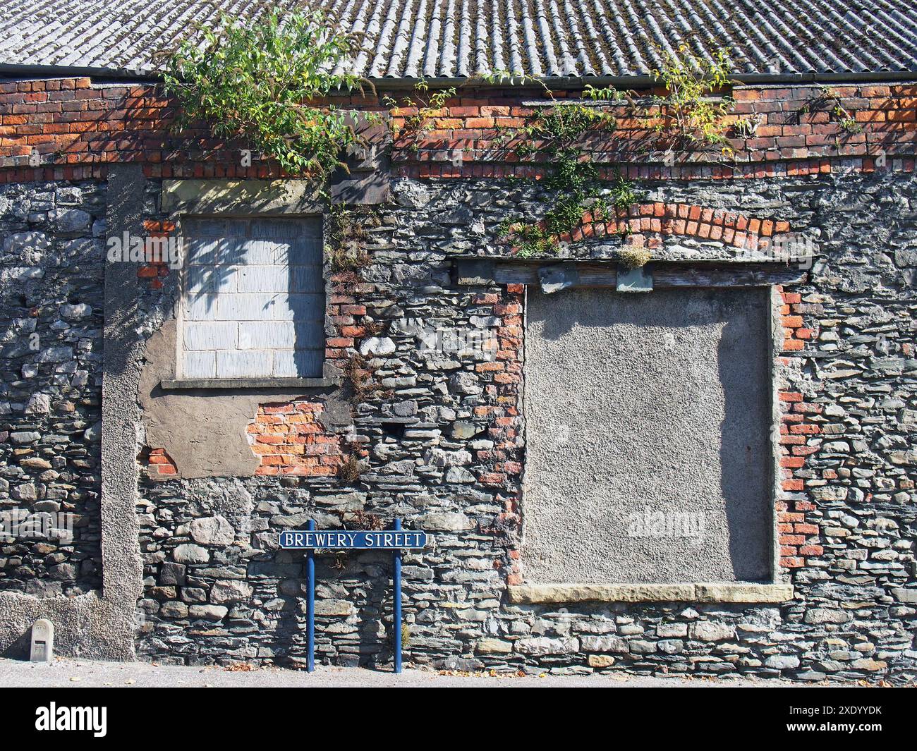 Derelict old stone building with blocked up windows, weeds growing from ...