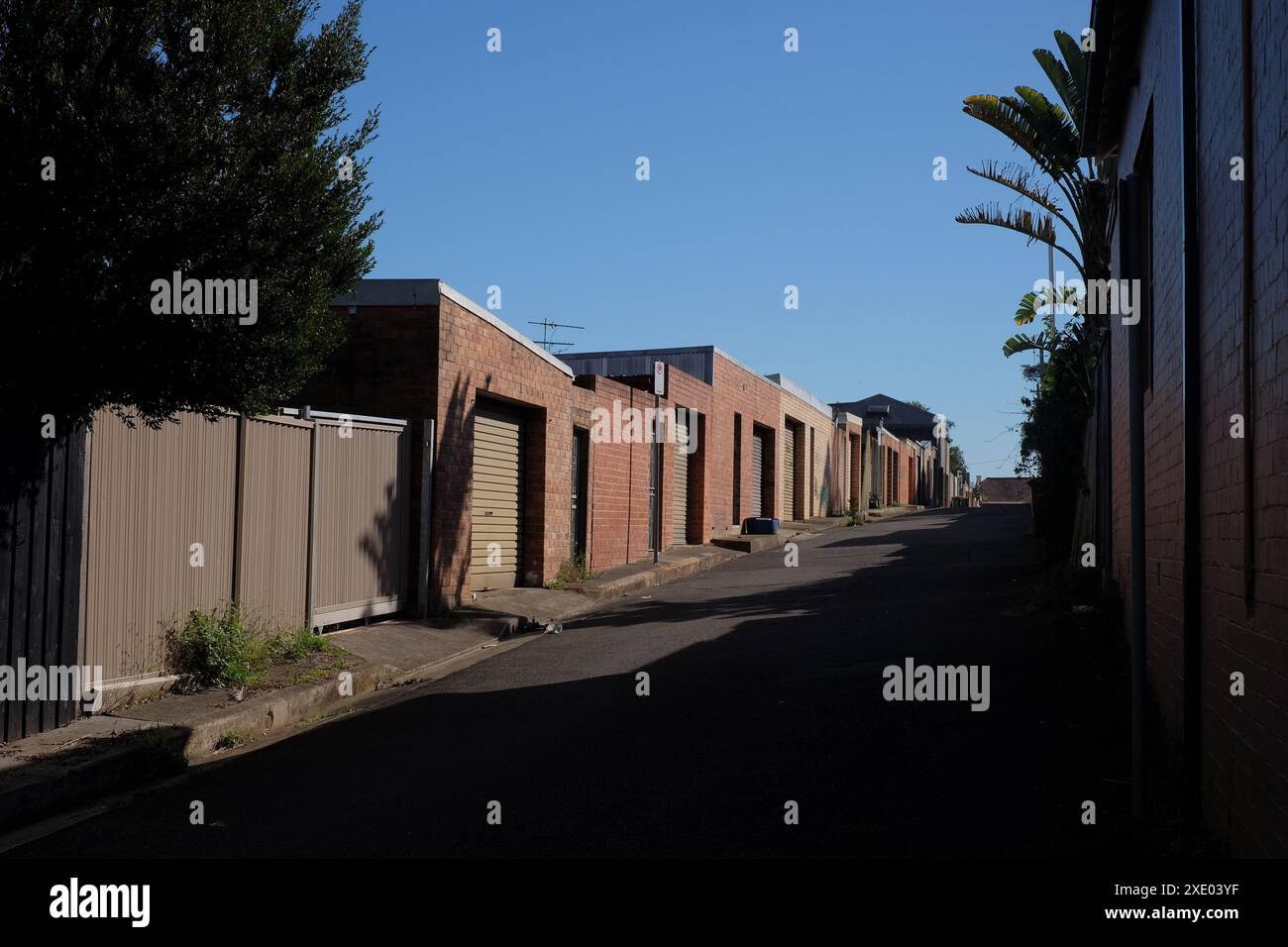 Brick garages with metal roller doors in full sun line a back lane of ...