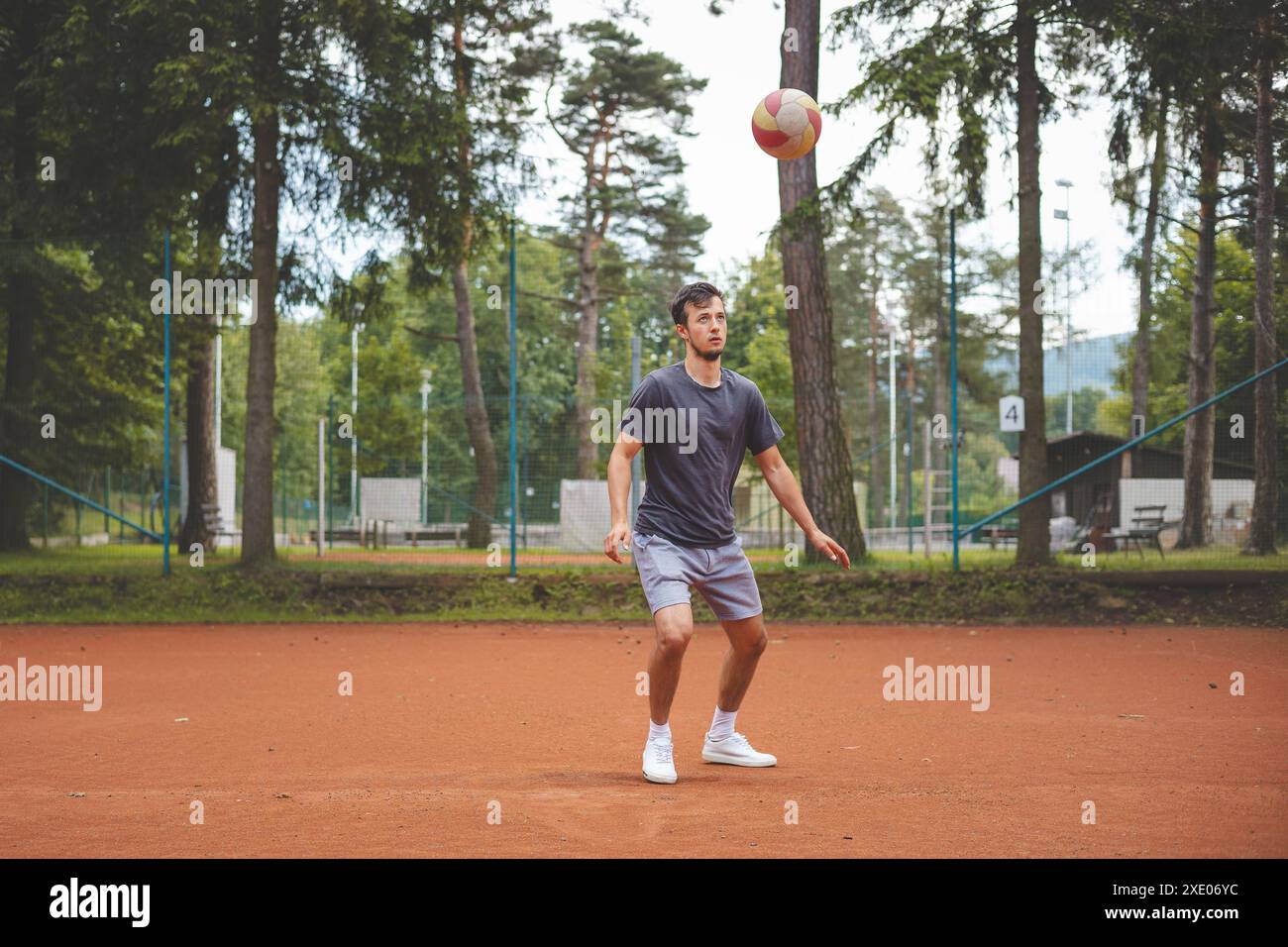 Soccer player in 20s plays with a balloon on a clay court. Amateur ...