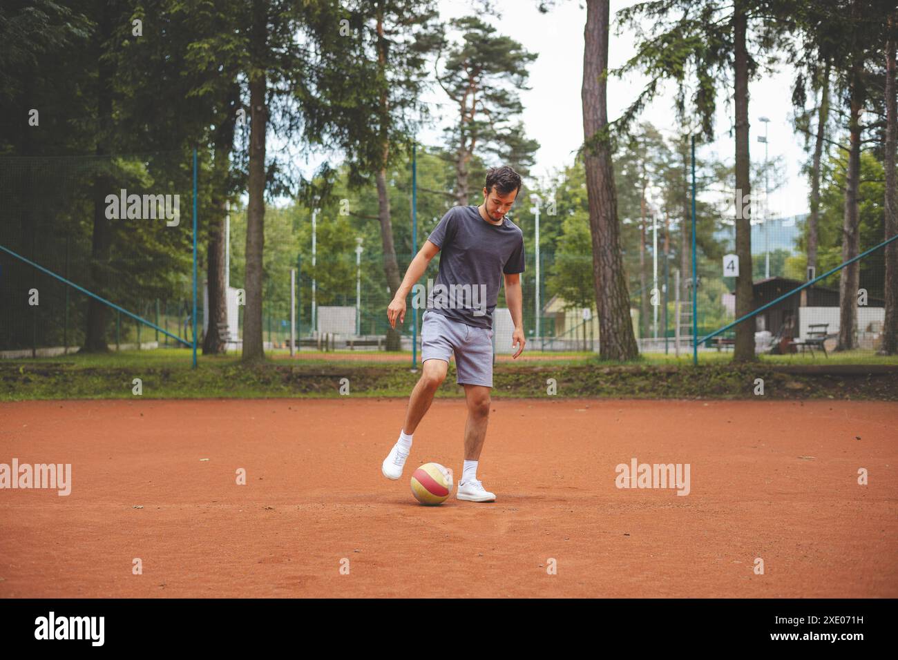 Soccer player in 20s plays with a balloon on a clay court. Amateur ...